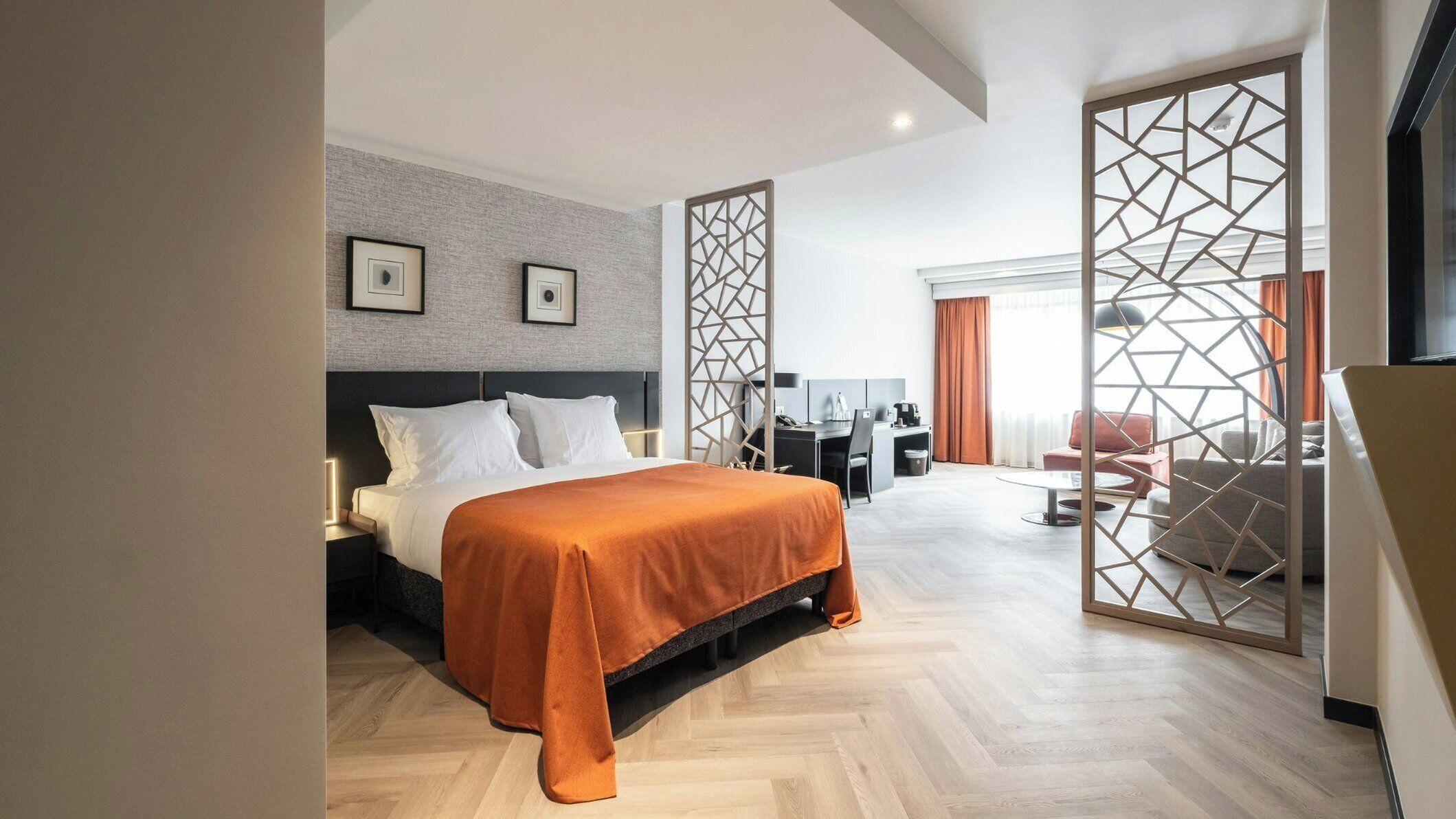 Quarto de hotel moderno com cama, escrivaninha e área de estar.