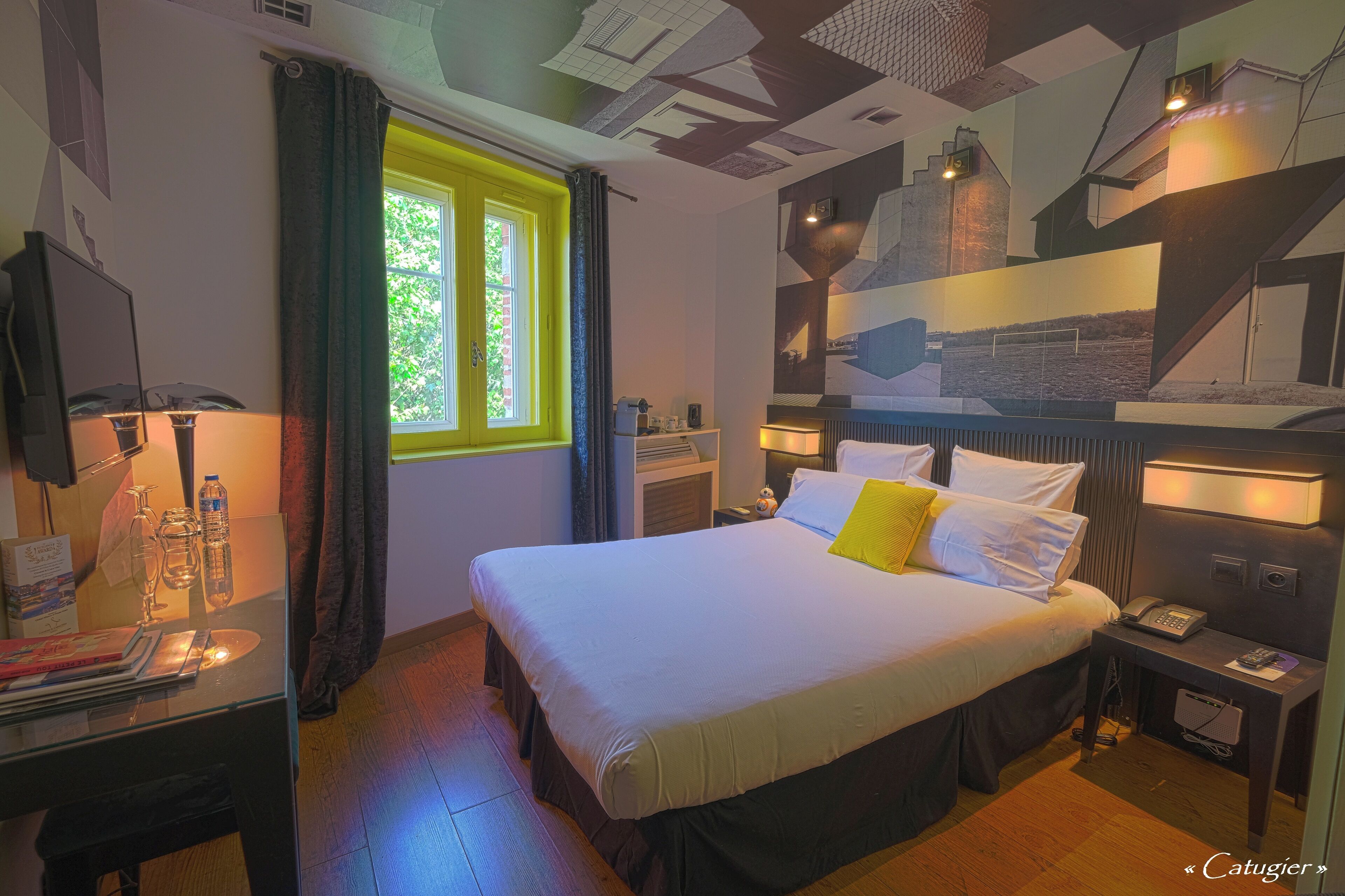 Quarto de hotel com cama, mesas de cabeceira, escrivaninha, janela com cortinas, televisão na parede e um quadro.
