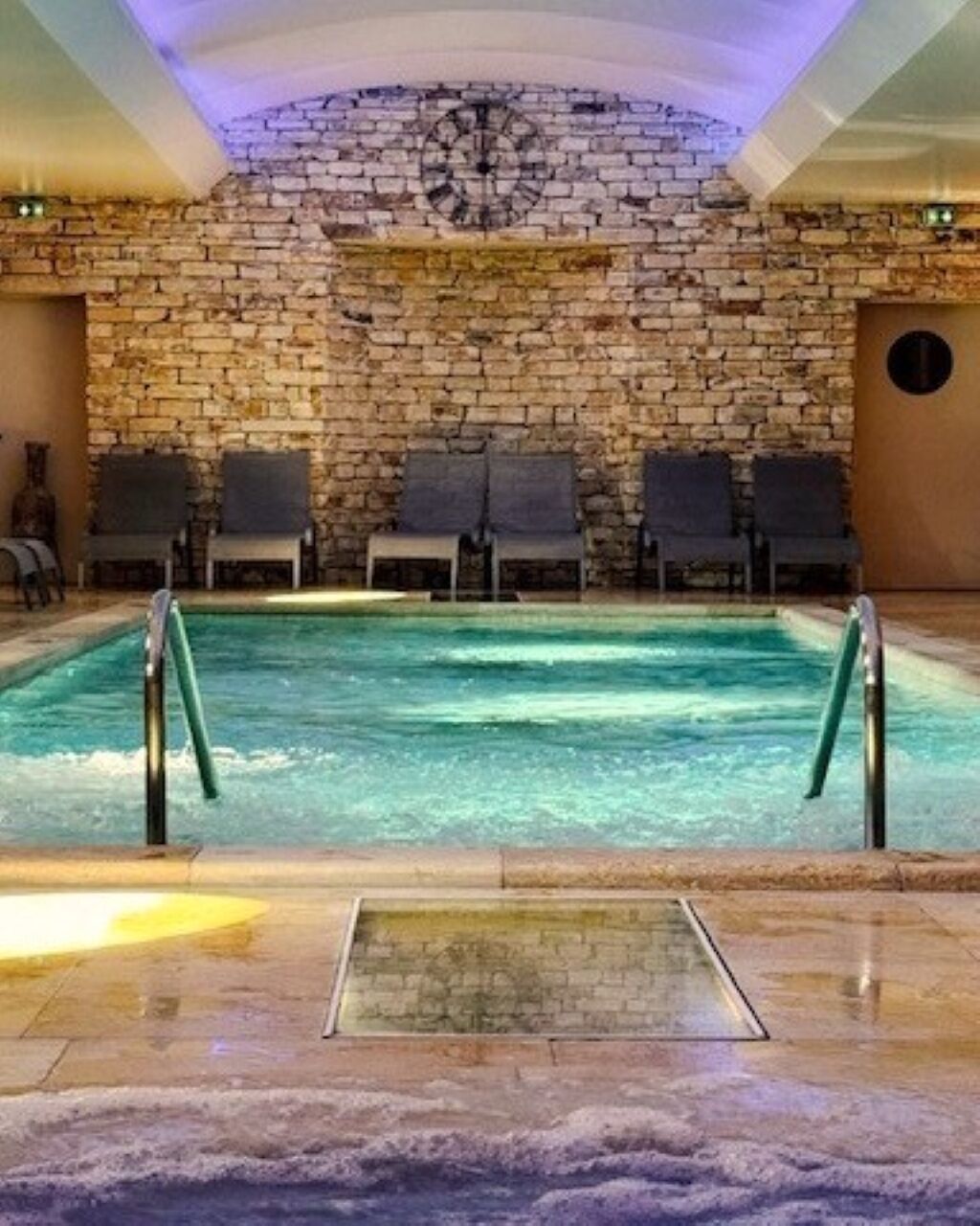 Piscina com paredes de pedra e espreguiçadeiras.