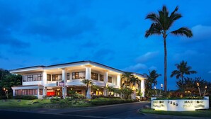 Um hotel moderno com uma entrada ampla, palmeiras e uma placa indicando ser o Maui Coast Hotel.