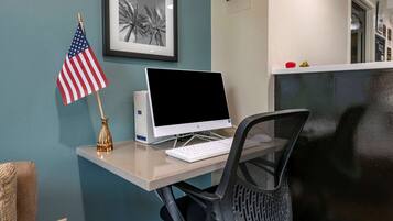 Uma mesa com um computador, uma bandeira americana e um quadro na parede.