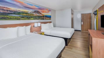 Quarto de hotel com duas camas, uma cabeceira de madeira, uma grande pintura de paisagem, uma escrivaninha de madeira e uma televisão.