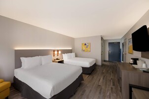 Quarto de hotel com uma cama grande, duas camas menores, uma escrivaninha, uma cadeira, máquina de café e televisão de tela plana.