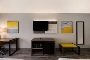Quarto de hotel com escrivaninha, pequeno espaço de cozinha, cama e obras de arte nas paredes.