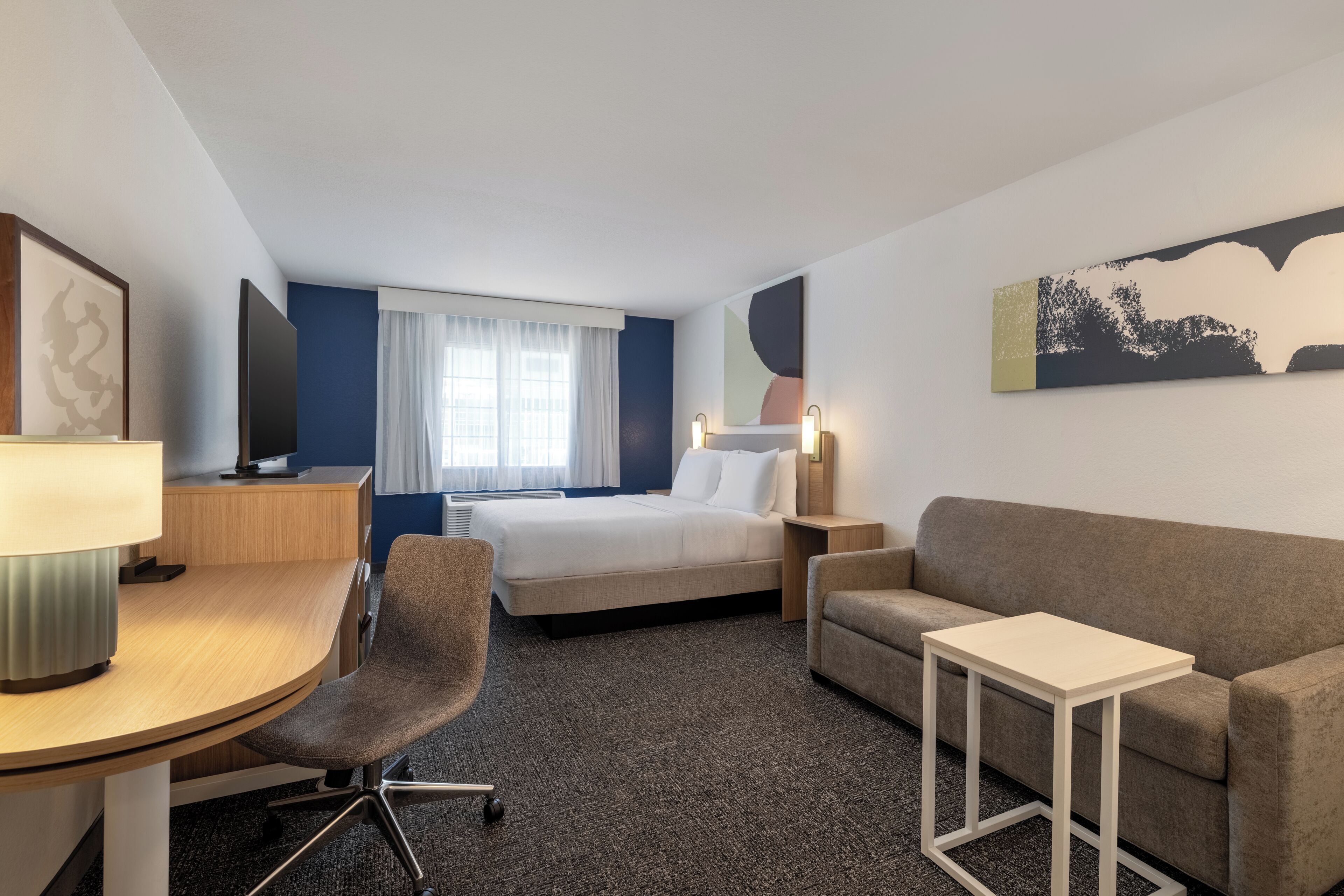 Quarto de hotel com cama, escrivaninha, cadeira, sofá e mesinha.