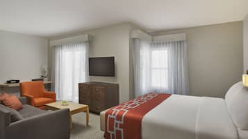 Quarto de hotel com cama, sofá, televisão, escrivaninha e cadeira.