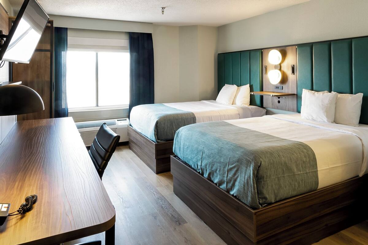 Quarto de hotel com duas camas, uma escrivaninha e uma janela com cortinas.