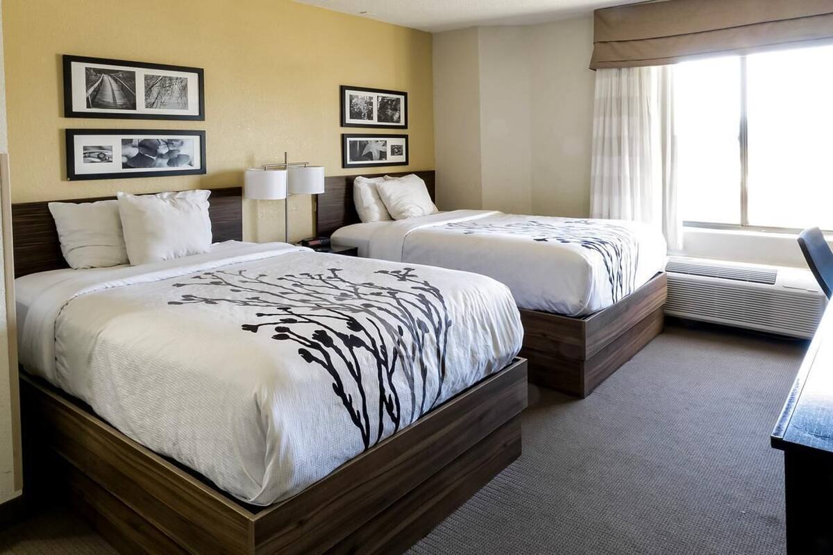 Quarto de hotel com duas camas, uma escrivaninha e uma janela com cortinas.