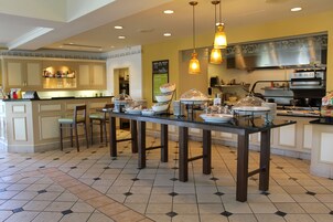 Disposição de buffet com diversas estações de serviço, área de cozinha e piso ladrilhado.