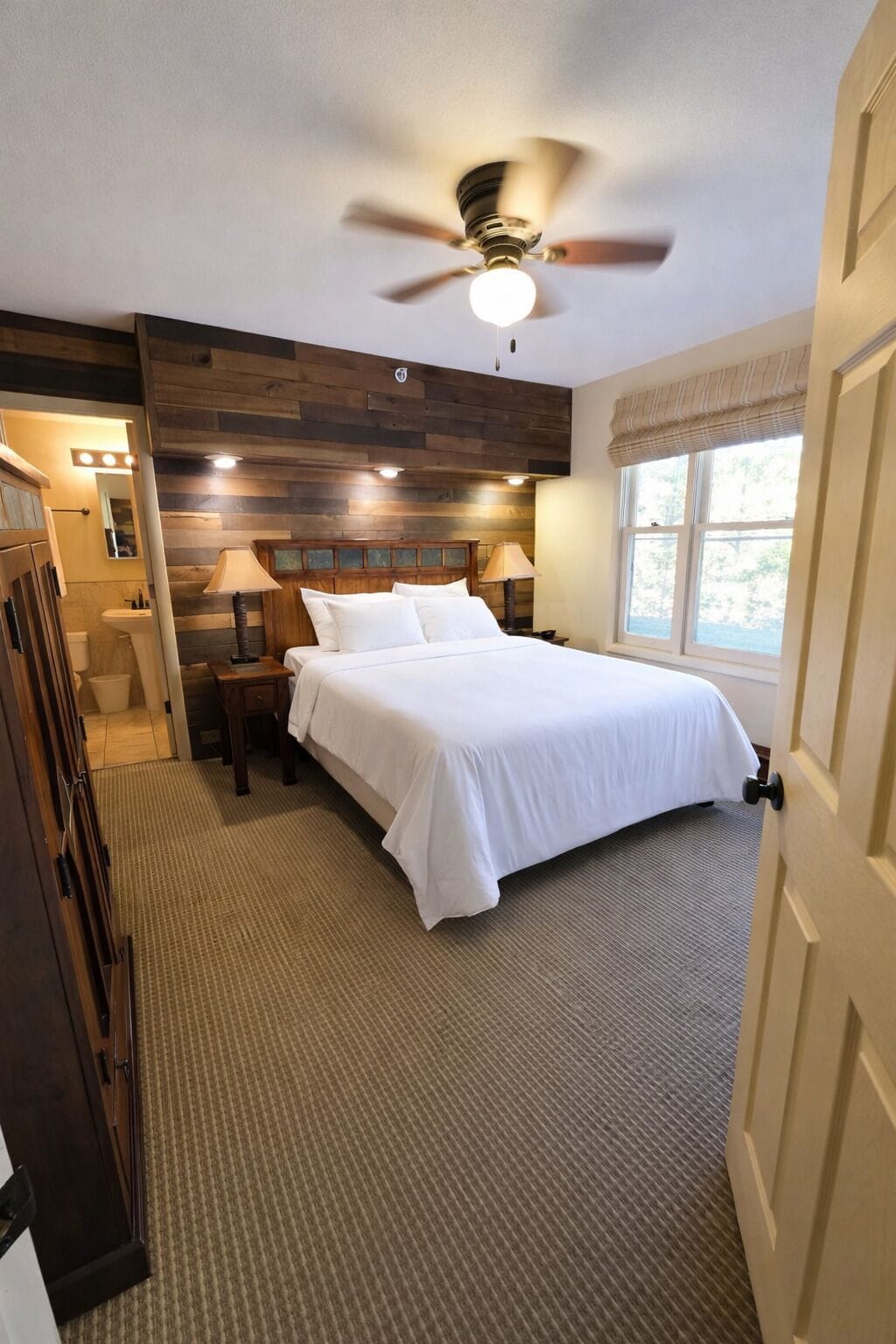 Um quarto com cama, ventilador de teto, janela e painel de parede de madeira.