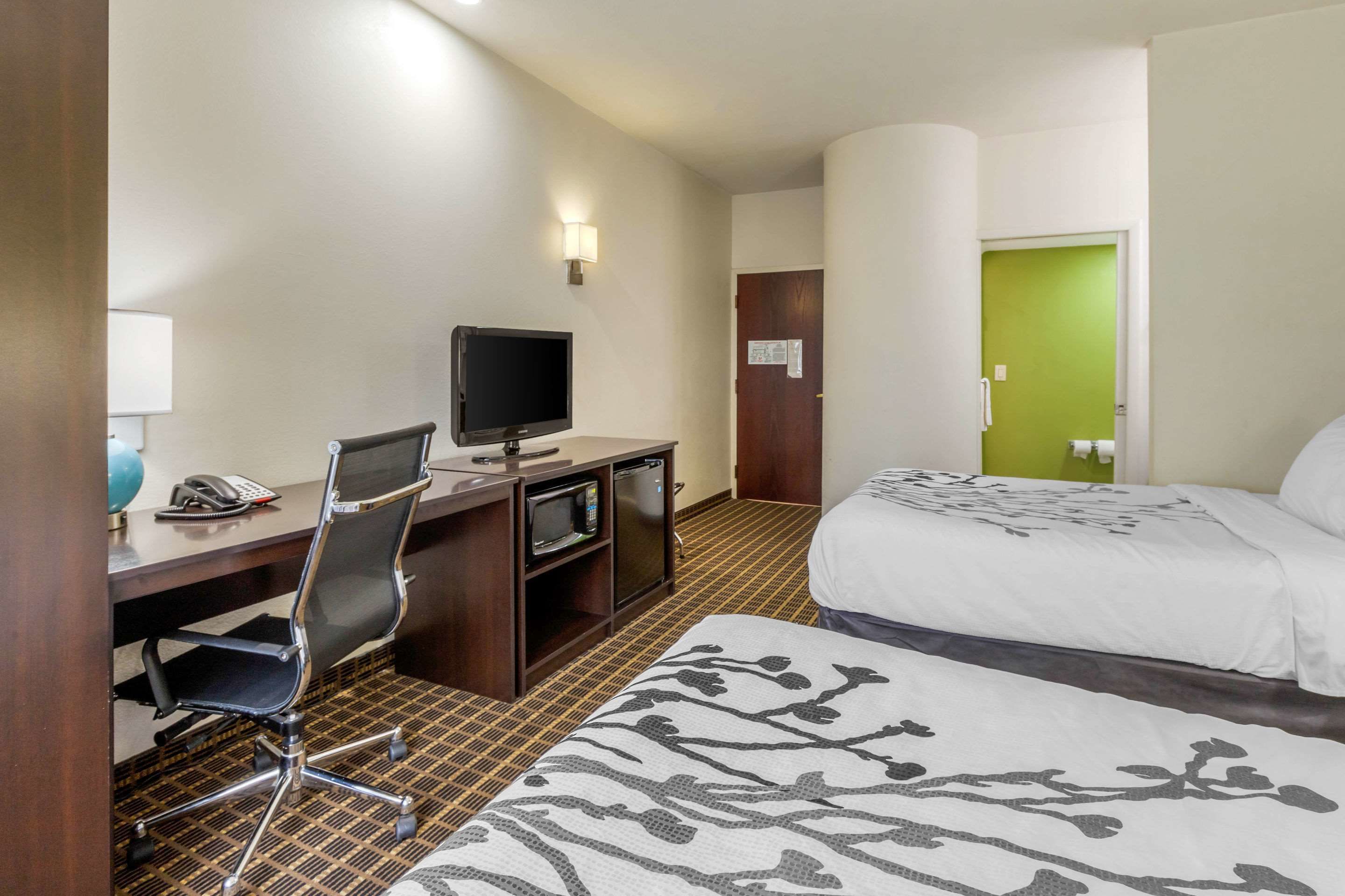 Quarto de hotel com cama, escrivaninha com computador, cadeira, telefone e micro-ondas.