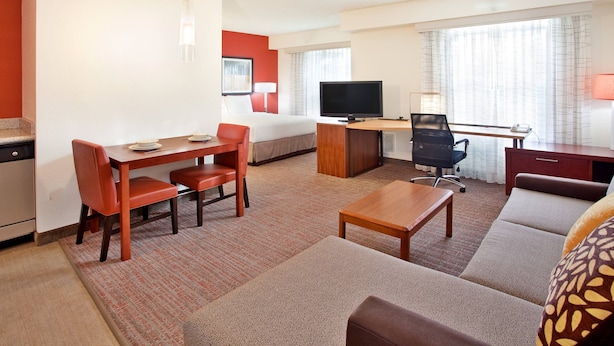 Quarto de hotel com área de refeições, televisão, escrivaninha e sofá.