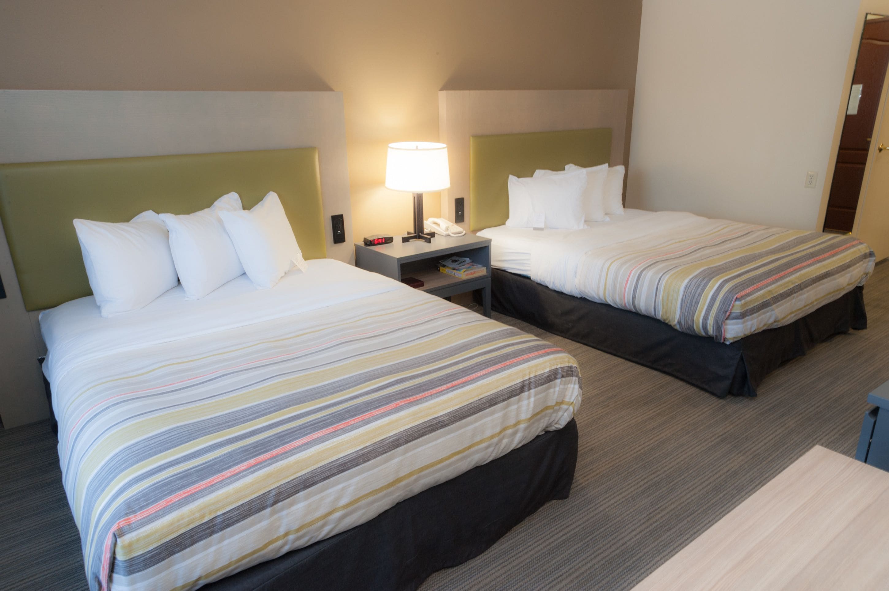Quarto de hotel com duas camas, cada uma com uma colcha listrada, uma mesinha de cabeceira com abajur e telefone.