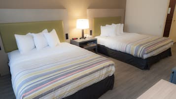 Quarto de hotel com duas camas, cada uma com uma colcha listrada, uma mesinha de cabeceira com abajur e telefone.