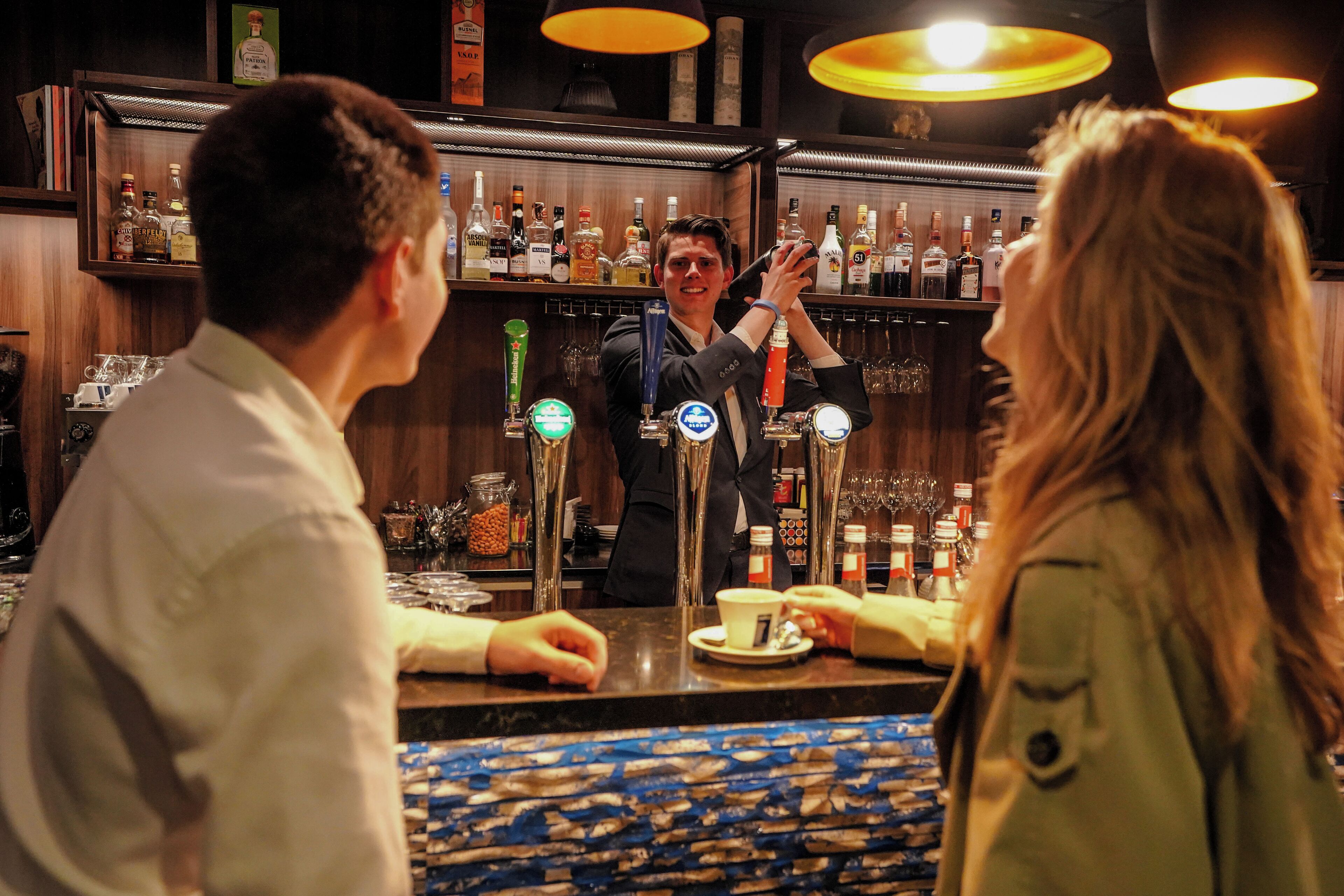 Uma área de bar com um bartender, um balcão e prateleiras cheias de garrafas.