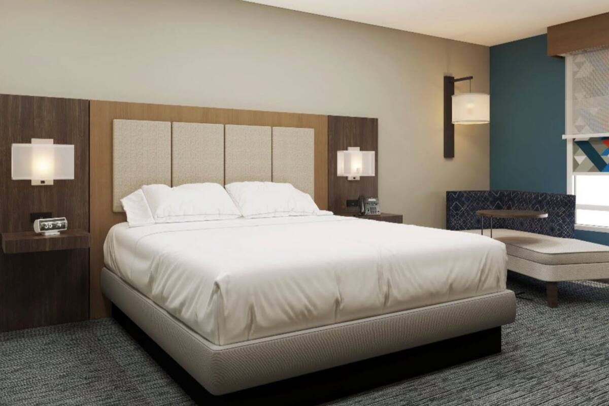 Quarto de hotel com uma cama grande, duas mesas de cabeceira com luminárias, uma pequena escrivaninha e uma cadeira.