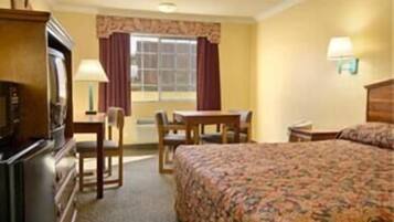 Quarto de hotel com cama, escrivaninha, cadeira, televisão e janela com cortinas.