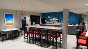 Um café moderno com balcão central, cadeiras estofadas em vermelho e bancada branca.