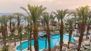 Resort com uma piscina grande rodeada por palmeiras e espreguiçadeiras.