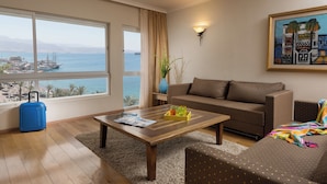 Sala de estar com vista para o mar, um sofá, uma mesa de centro e uma mala azul.