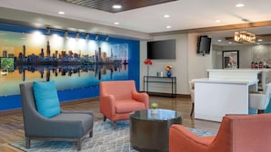 Um hall de hotel moderno com um mural de paisagem urbana, assentos confortáveis, um balcão de recepção e um bar.