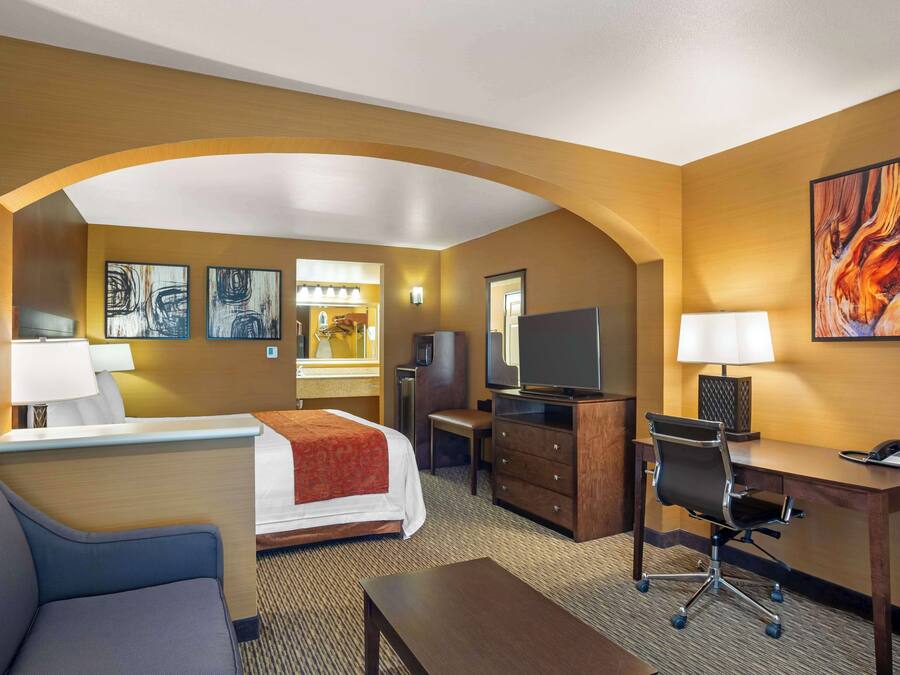 Quarto de hotel com cama, escrivaninha, cadeira, televisão e obras de arte nas paredes.