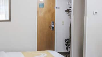 Quarto de hotel com porta de madeira, um cabideiro e um termostato na parede.