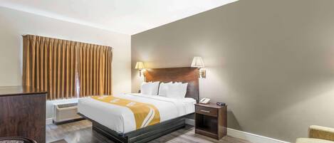 Quarto de hotel com cama, mesa de cabeceira, abajur e escrivaninha.