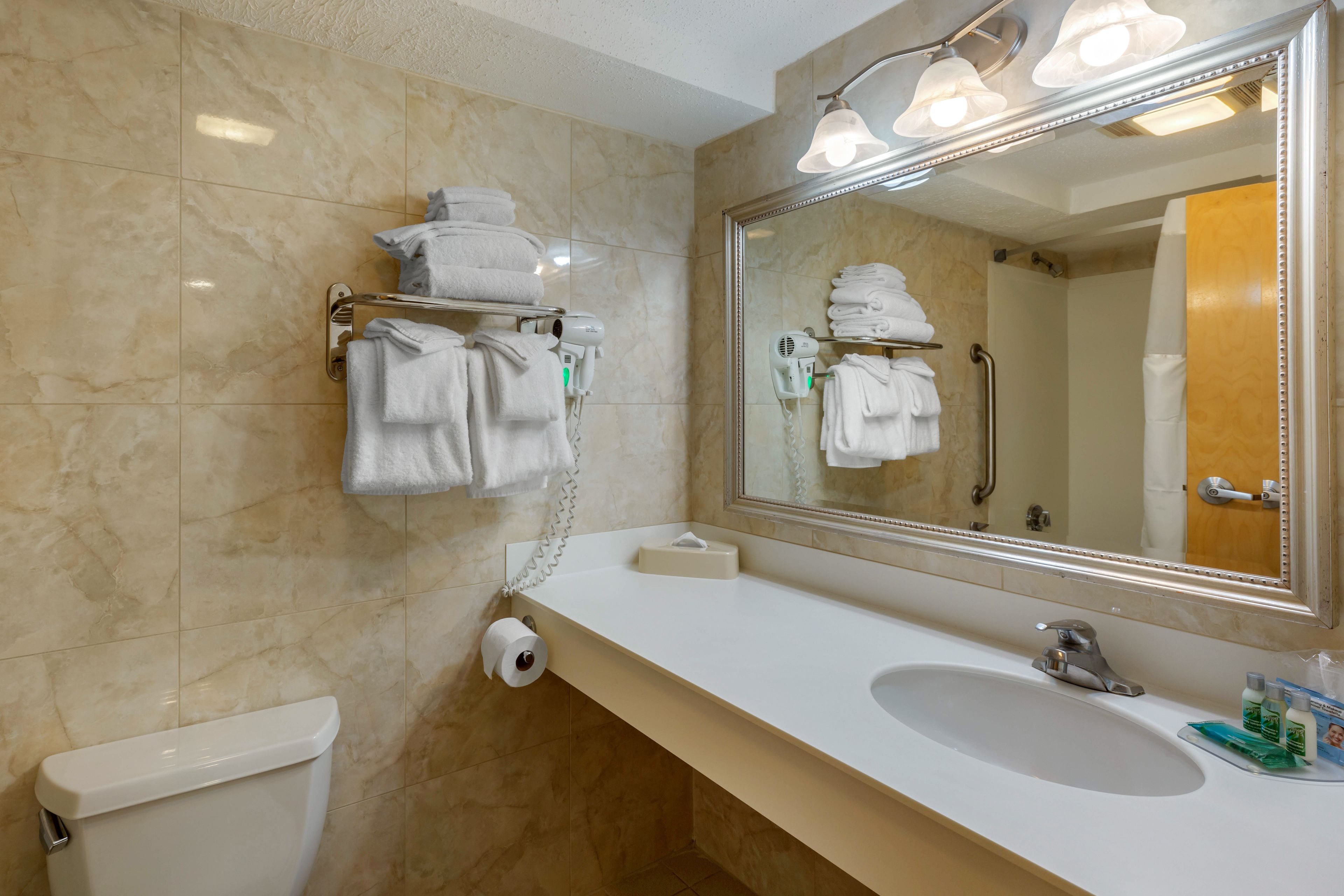 Casa de banho com lavatório branco, espelho e porta-toalhas com toalhas dobradas.