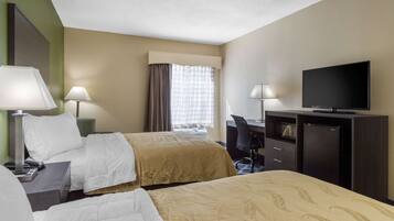 Quarto de hotel com duas camas, uma escrivaninha com computador, televisão e janela com cortinas.
