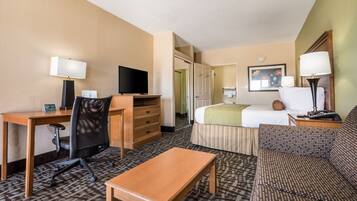 Quarto de hotel com escrivaninha, cadeira, televisão, cama, mesa de cabeceira, abajur e um quadro na parede.