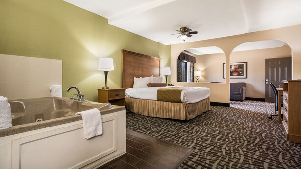 Quarto de hotel com uma banheira grande, uma cama com cabeceira de madeira, uma escrivaninha e uma cadeira.