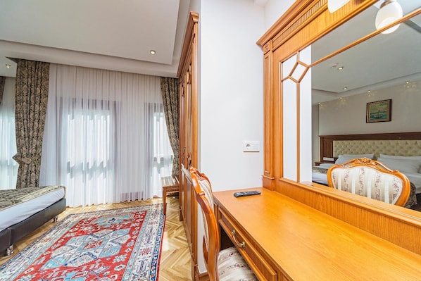 Quarto de hotel com uma cama grande, cômoda de madeira, espelho e tapete vermelho estampado.