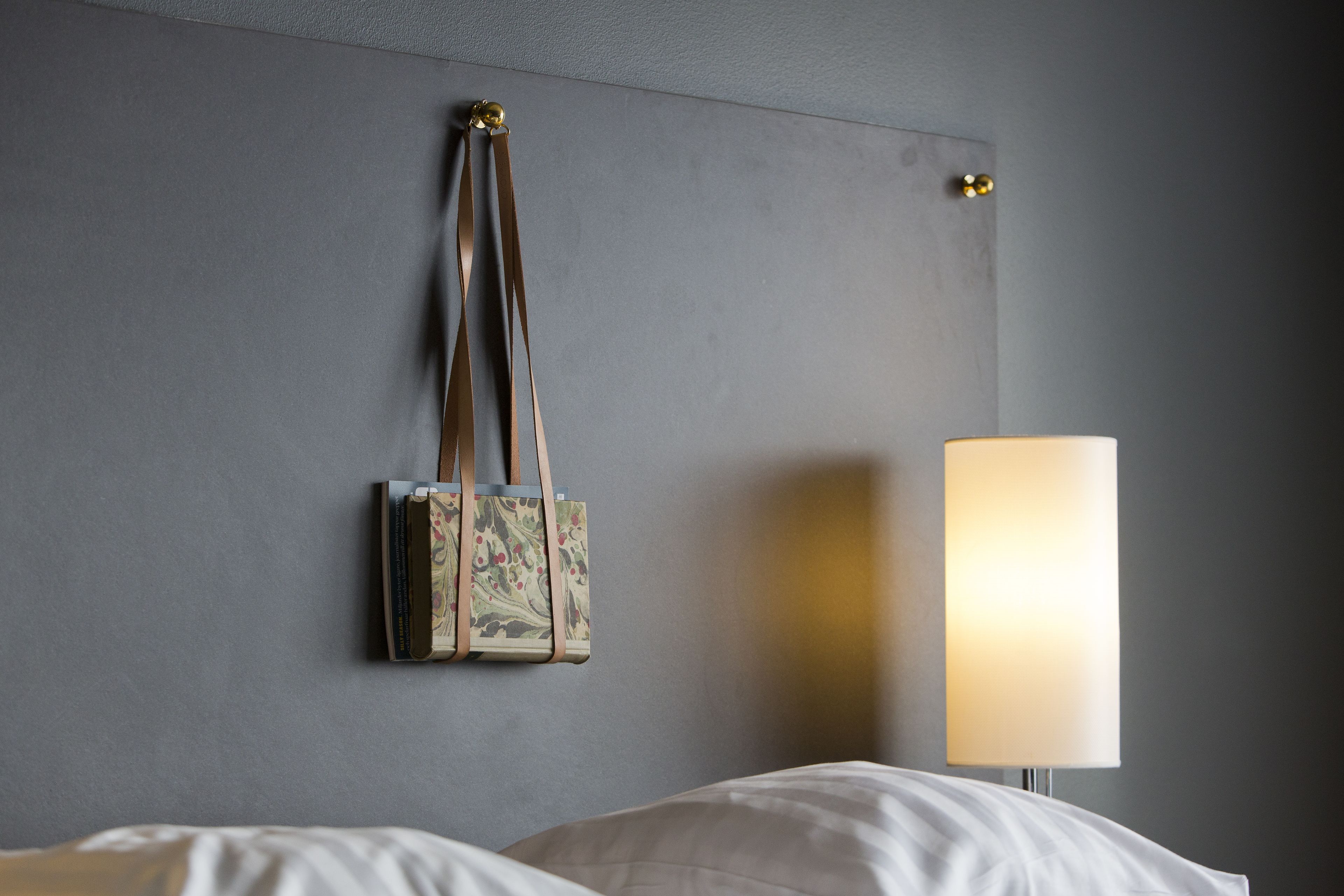 Quarto de hotel com uma cama, uma luminária na parede e uma bolsa decorativa pendurada.