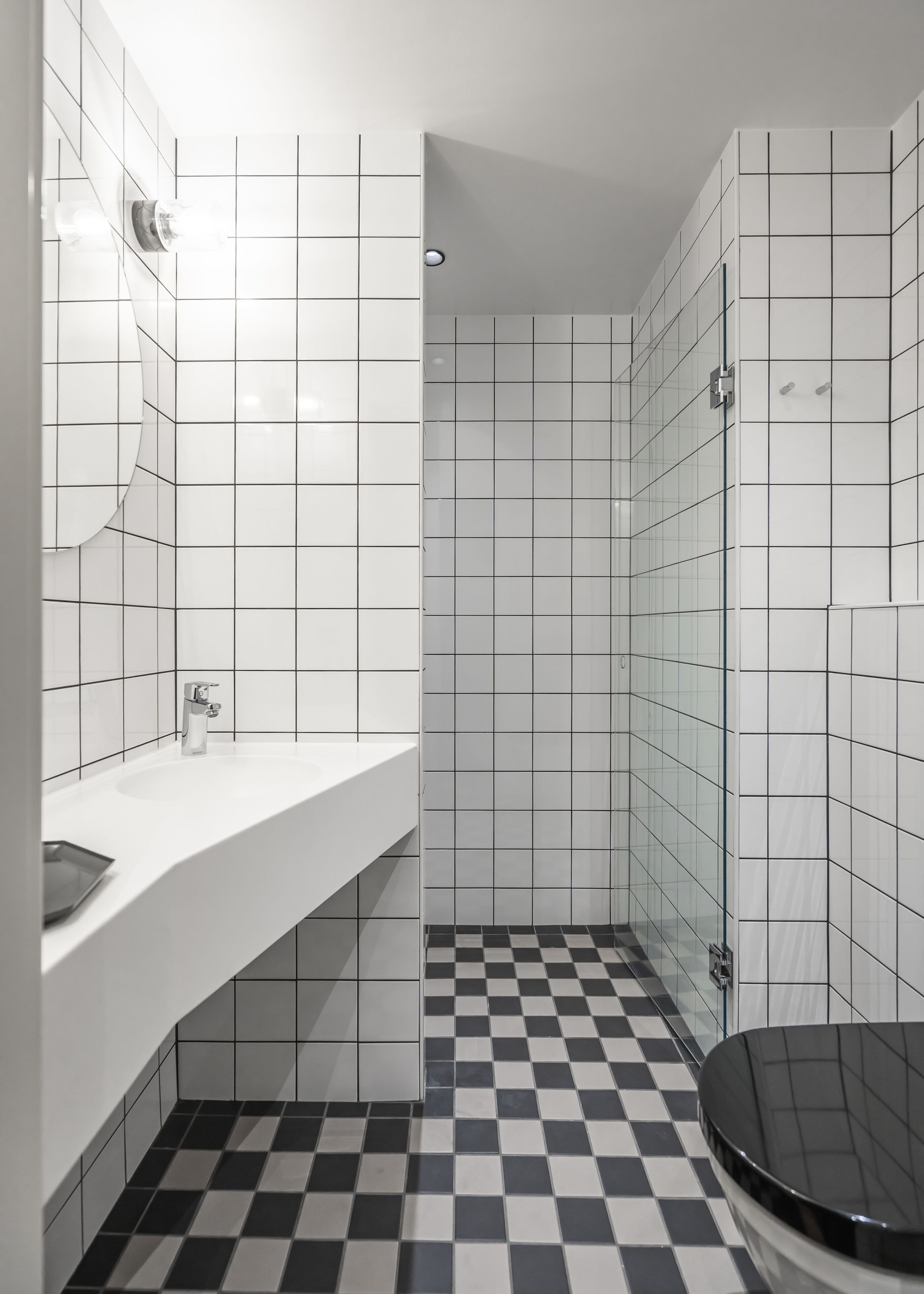Casa de banho moderna com azulejos brancos tipo metrô, chão xadrez preto e branco, pia branca e sanita preta.