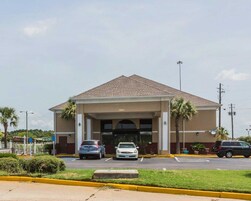 Um edifício com entrada coberta, estacionamento e palmeiras.