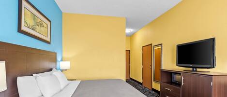 Quarto de hotel com uma cama, televisão, escrivaninha e um quadro na parede.