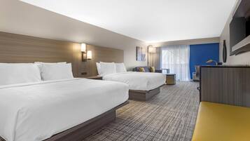 Quarto de hotel com duas camas, uma escrivaninha, uma cadeira, televisão e janela com cortinas.