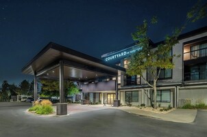 Entrada moderna de hotel com área externa coberta, uma placa indicando 'COURTYARD BY MARGIE' e um estacionamento.