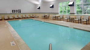 Piscina com espreguiçadeiras e mesas, placa indicando proibição de mergulho e vista para árvores através de grandes janelas.