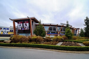 Um edifício moderno com placa de centro esportivo, cercado por jardins ajardinados e estacionamento.