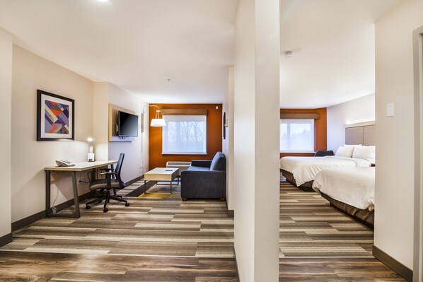 Quarto de hotel com escrivaninha, cadeira, sofá e duas camas.