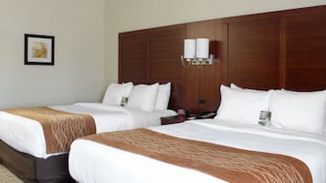 Quarto de hotel com duas camas, uma cabeceira de madeira, um criado-mudo com abajur e um quadro na parede.