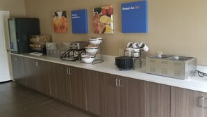 Uma mesa de pequeno-almoço com frigorífico, máquina de café e diversas opções para o pequeno-almoço.