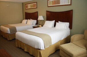 Quarto de hotel com duas camas, mesa de cabeceira, abajur e uma cadeira.