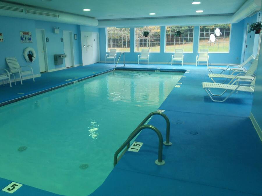 Piscina interna com água azul cristalina, cadeiras brancas na beira da piscina e vista para árvores lá fora.