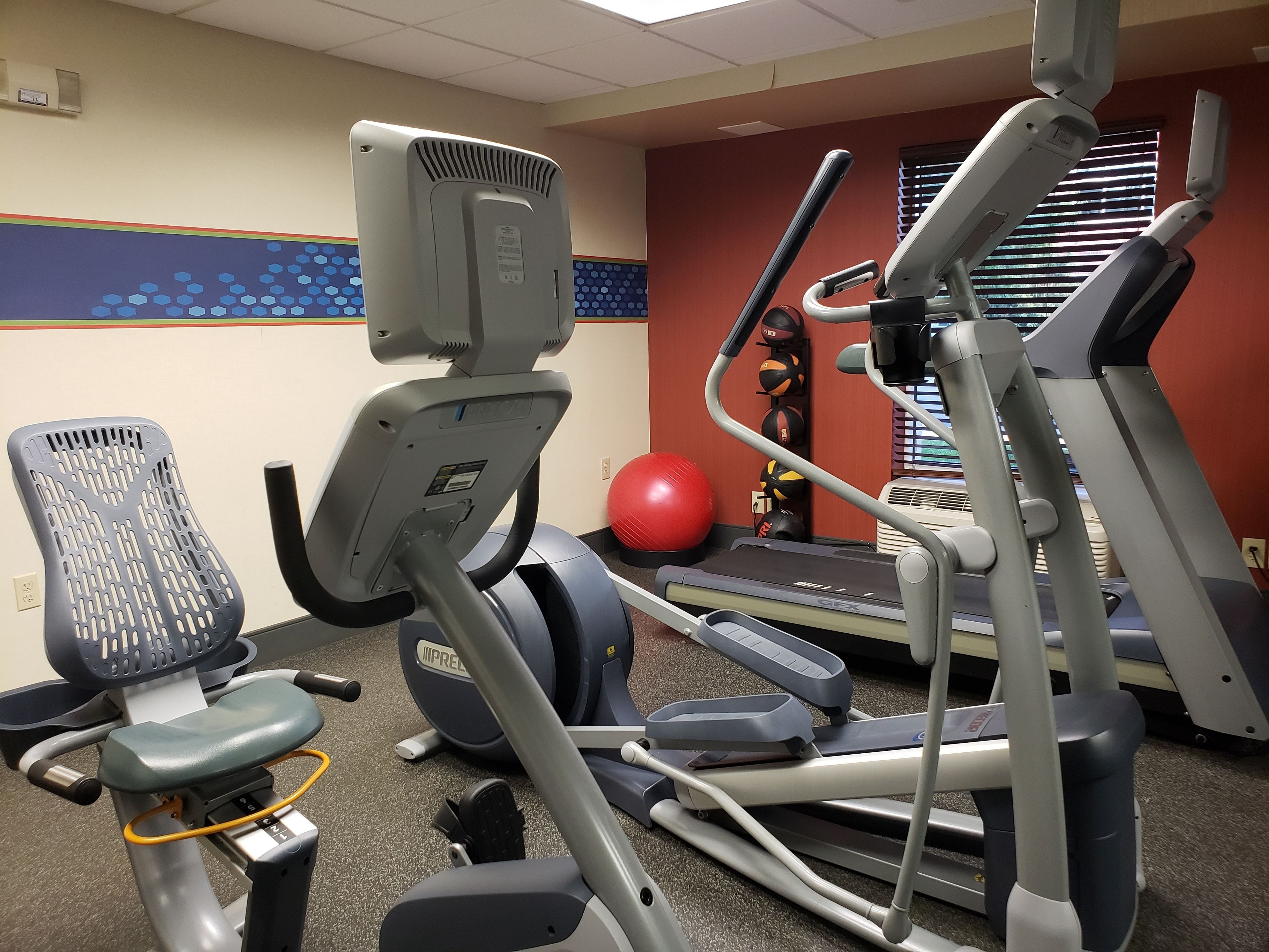 Uma academia com equipamentos de ginástica, incluindo esteira, elíptico e bicicleta ergométrica.