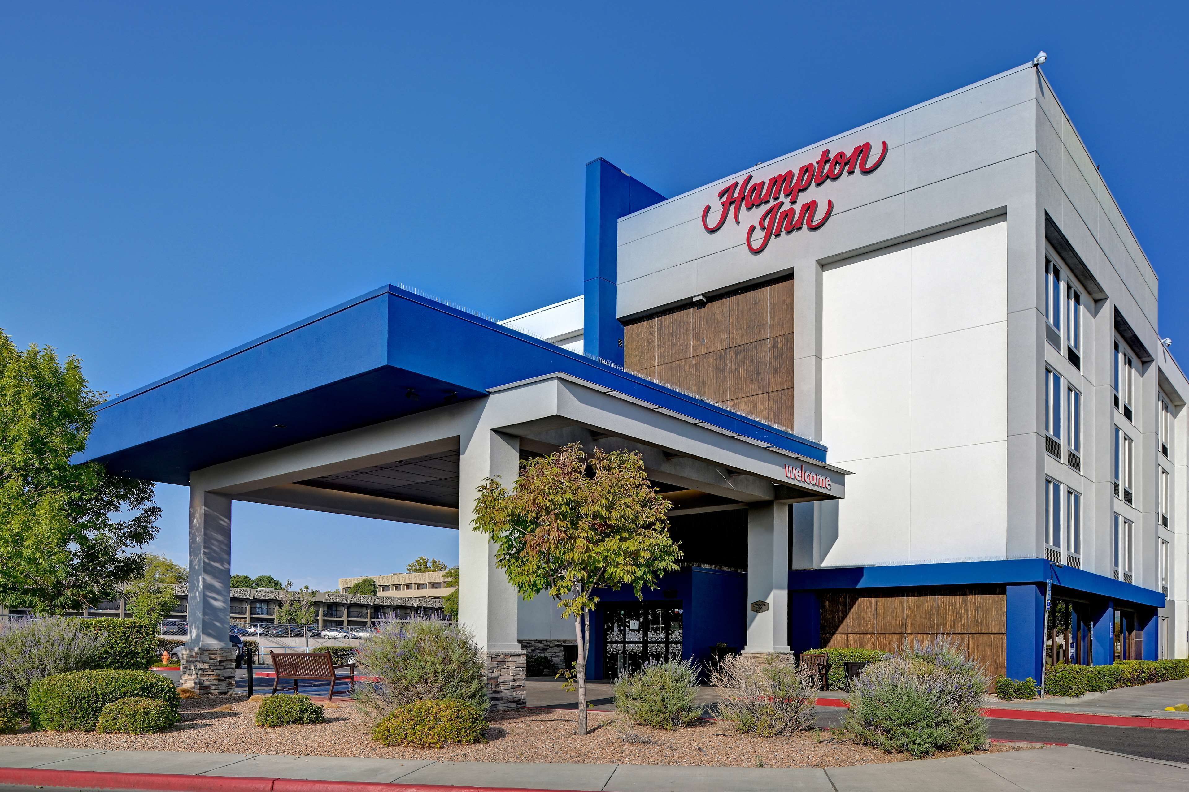 Um hotel Hampton Inn com design moderno, destacando uma paleta de cores azul e branca, uma área externa coberta e uma entrada convidativa.