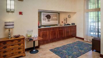 Uma área de recepção de hotel com um balcão de madeira, uma grande moldura com a imagem de um cão, um relógio e uma janela com cortinas.