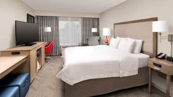 Quarto de hotel com uma cama grande, uma mesa com computador, televisão e uma cadeira vermelha.